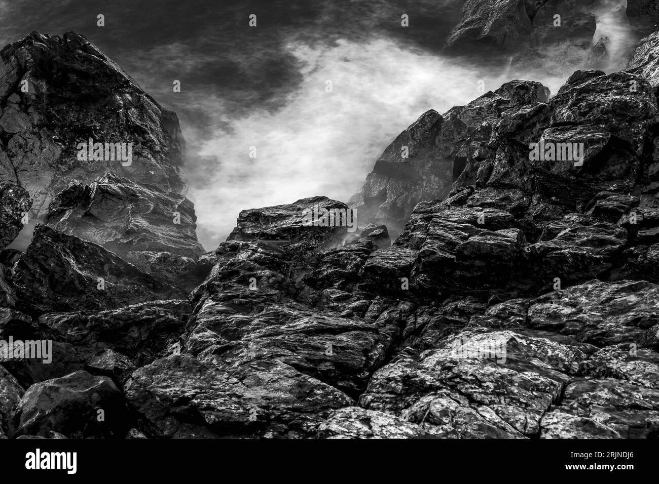 A dramatic grayscale landscape featuring wet rocks and a gathering ...