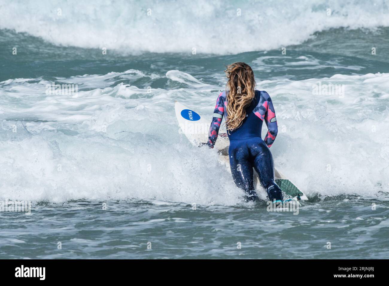 A female surfer on her surfboard making her way out to sea at Fistral ...