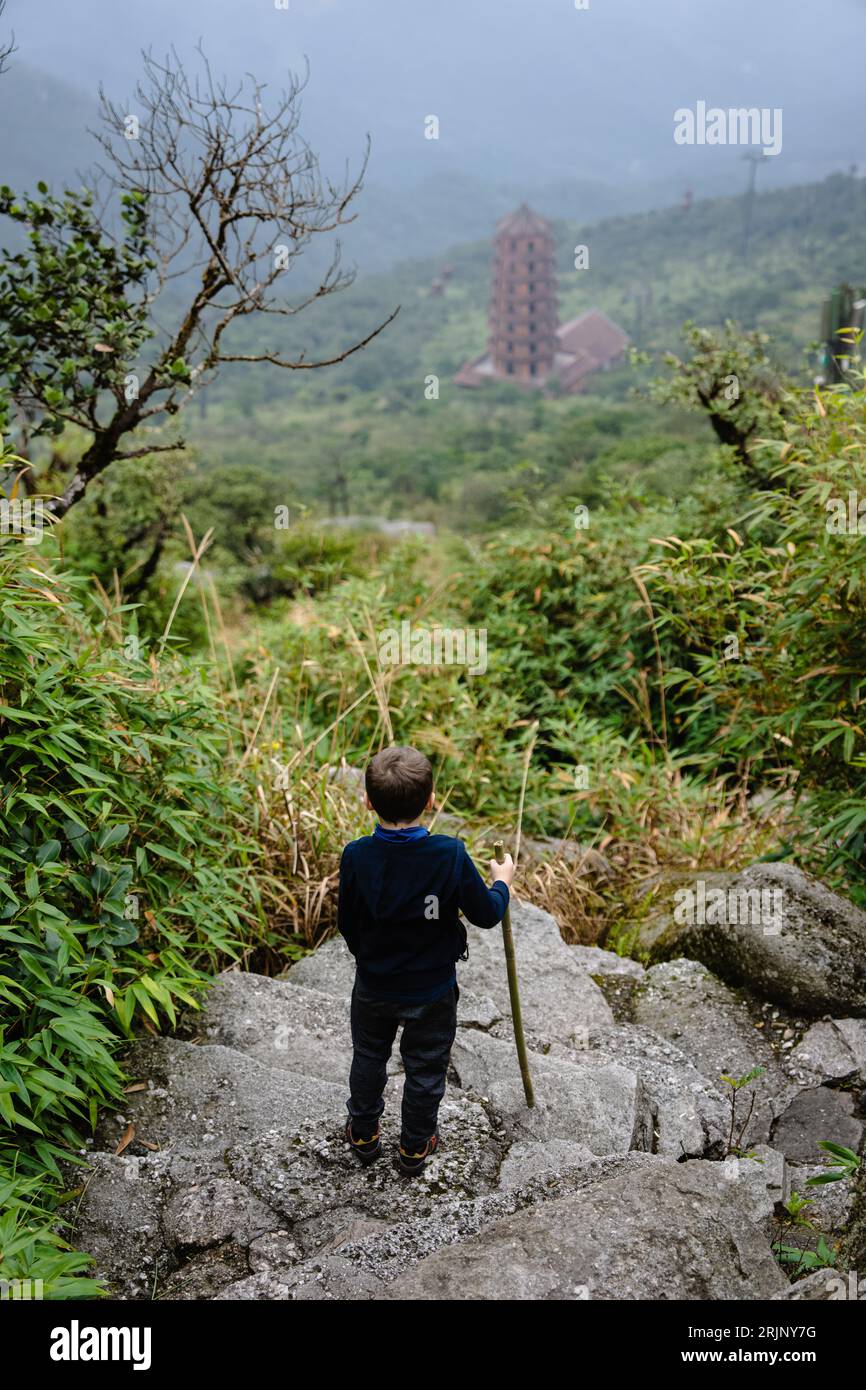 A young adventurous boy with a walking stick, looking out at the Yen Tu ...