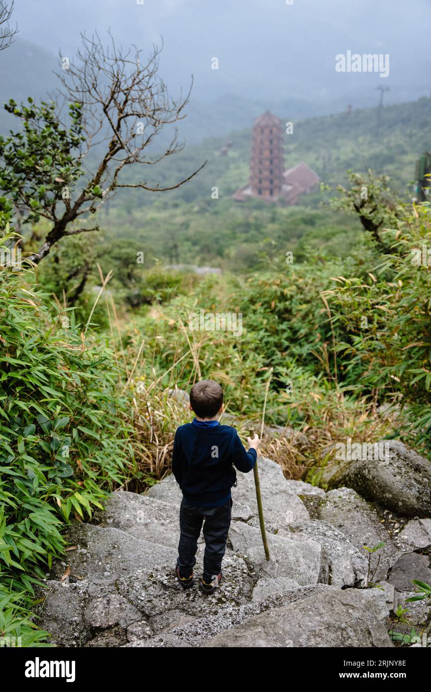 A young adventurous boy with a walking stick, looking out at the Yen Tu ...