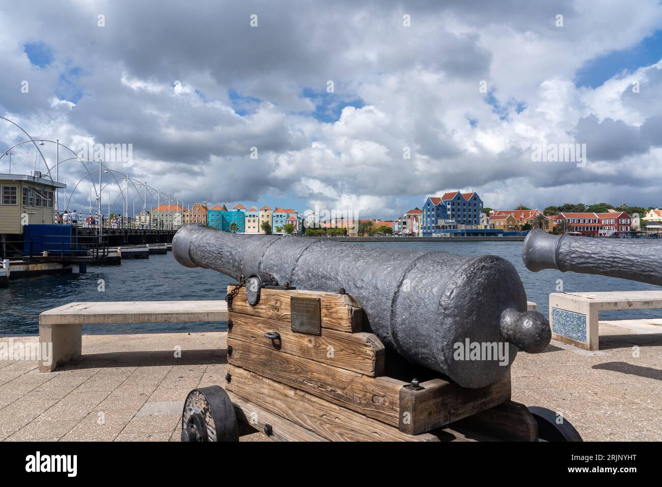 A historic cannon located on a dock against a backdrop of waterfront ...