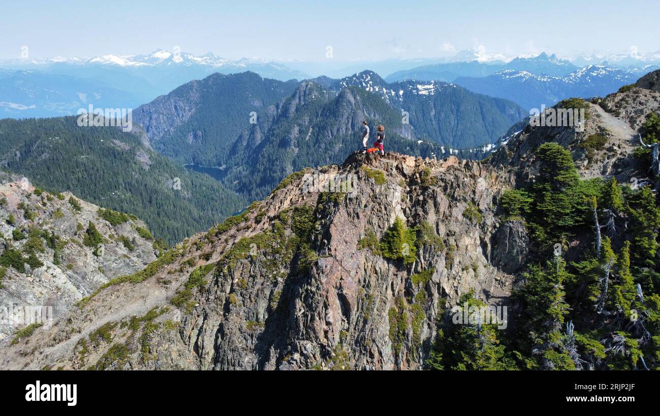 Two people stands together atop a majestic mountain, taking in the ...