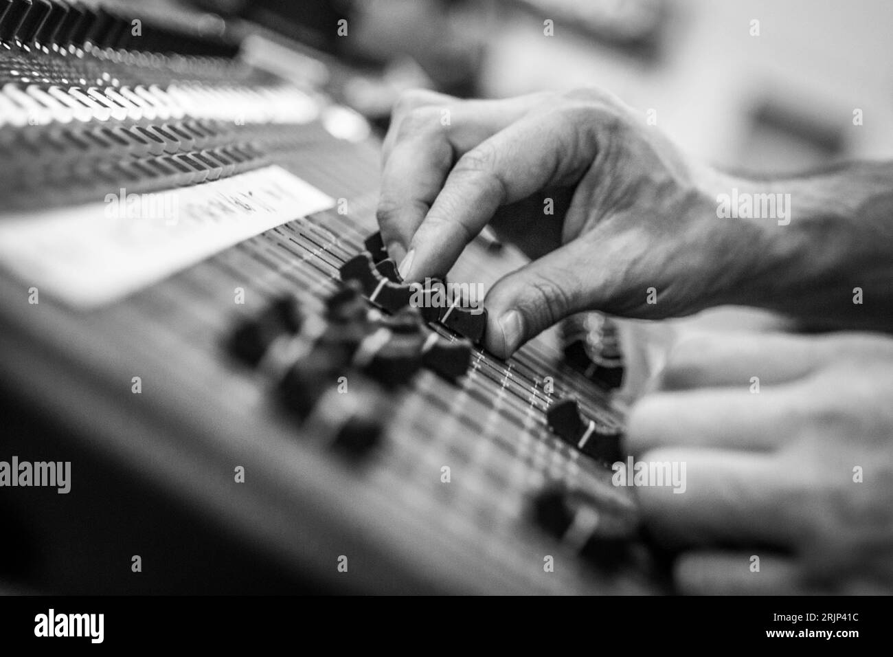 A person operating a mixing desk with their hands making adjustments to ...