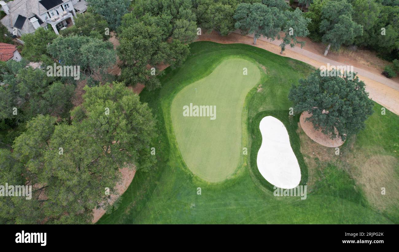 An aerial view of a golf course located in a city with lush trees ...