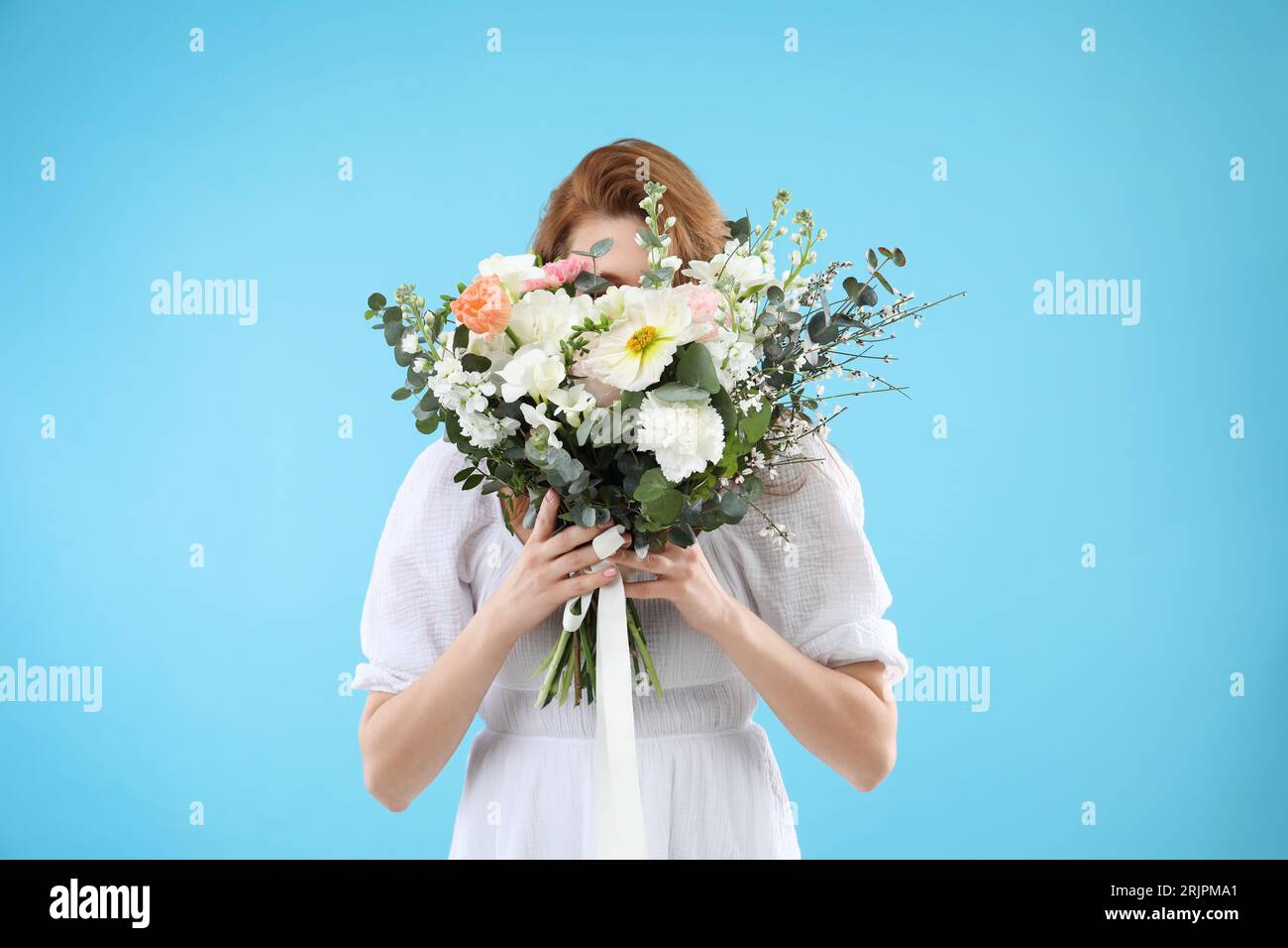 Woman covering her face with bouquet of beautiful flowers on light blue ...