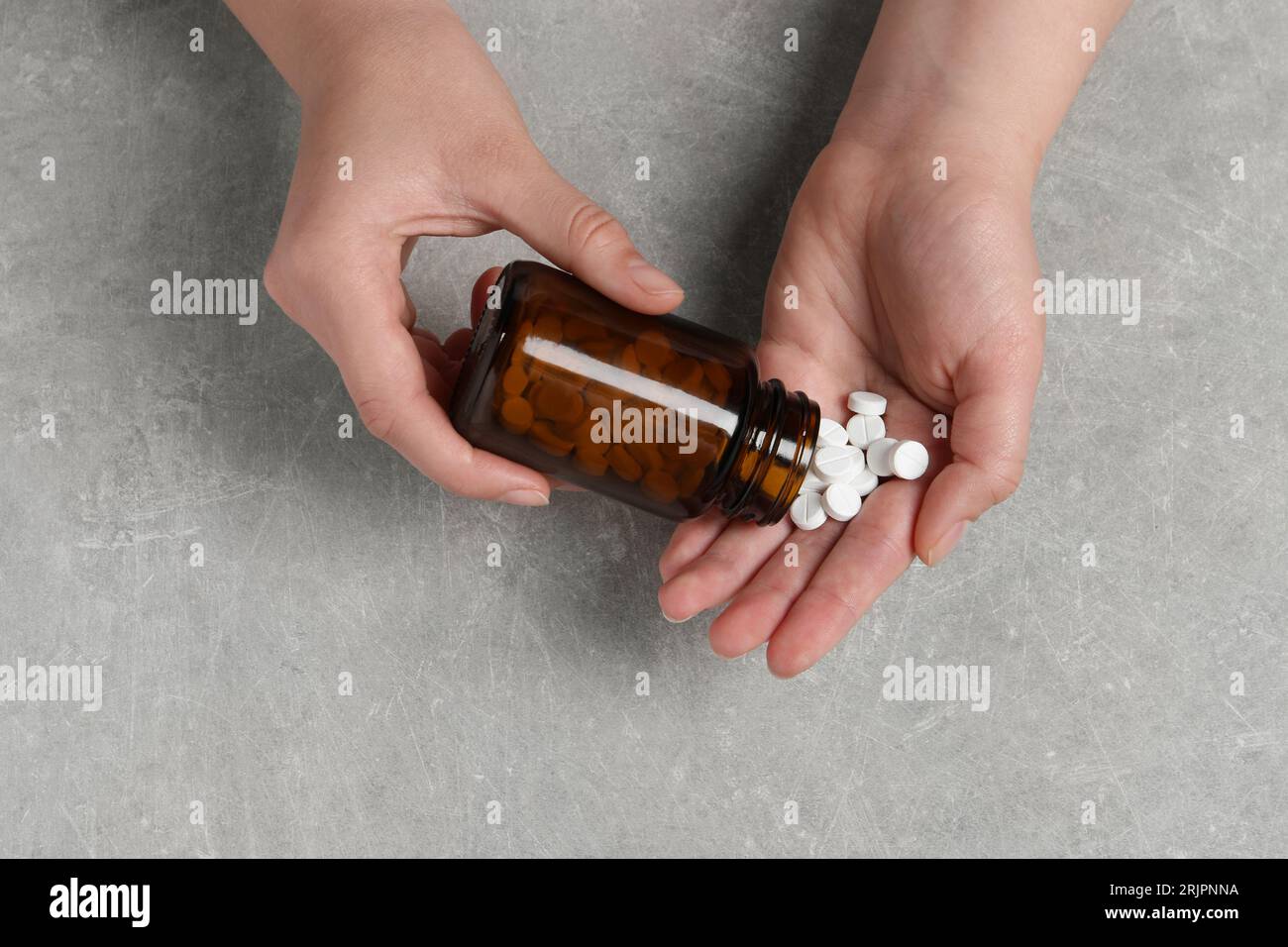 Woman pouring pills from bottle onto hand at light grey table, top view ...