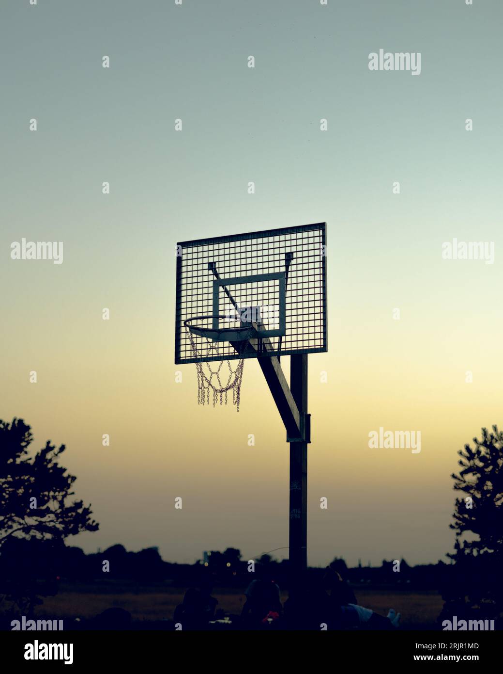 A basketball court illuminated by the glowing sun in the twilight sky ...