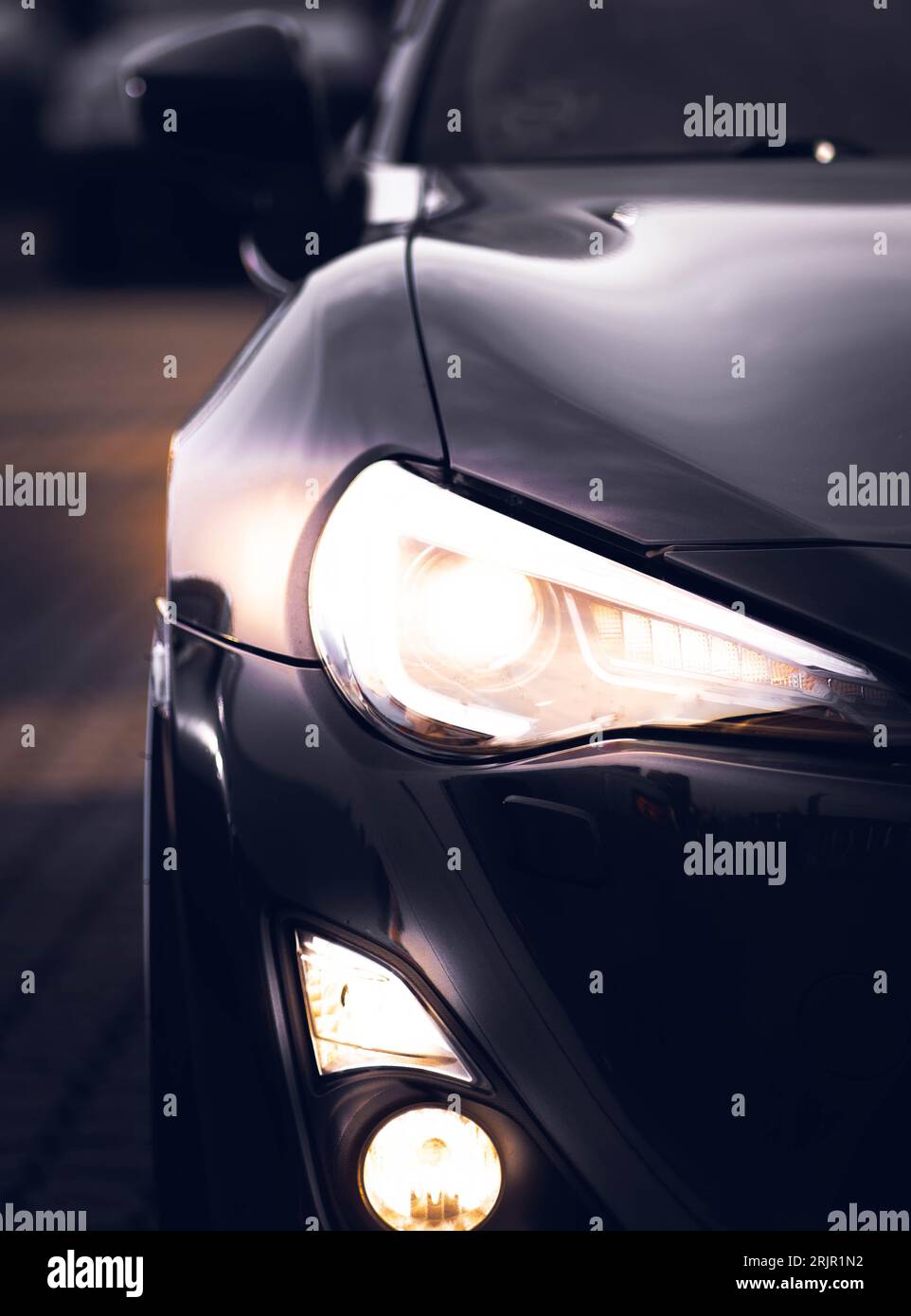 A close-up of a front view of a black car, its headlights and lights on ...