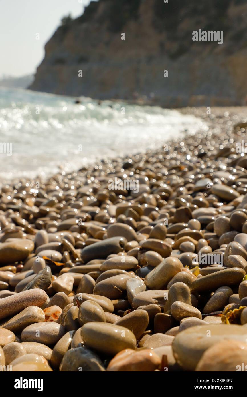 A sun-drenched beach in Alicante, Spain, featuring textured sea rocks ...