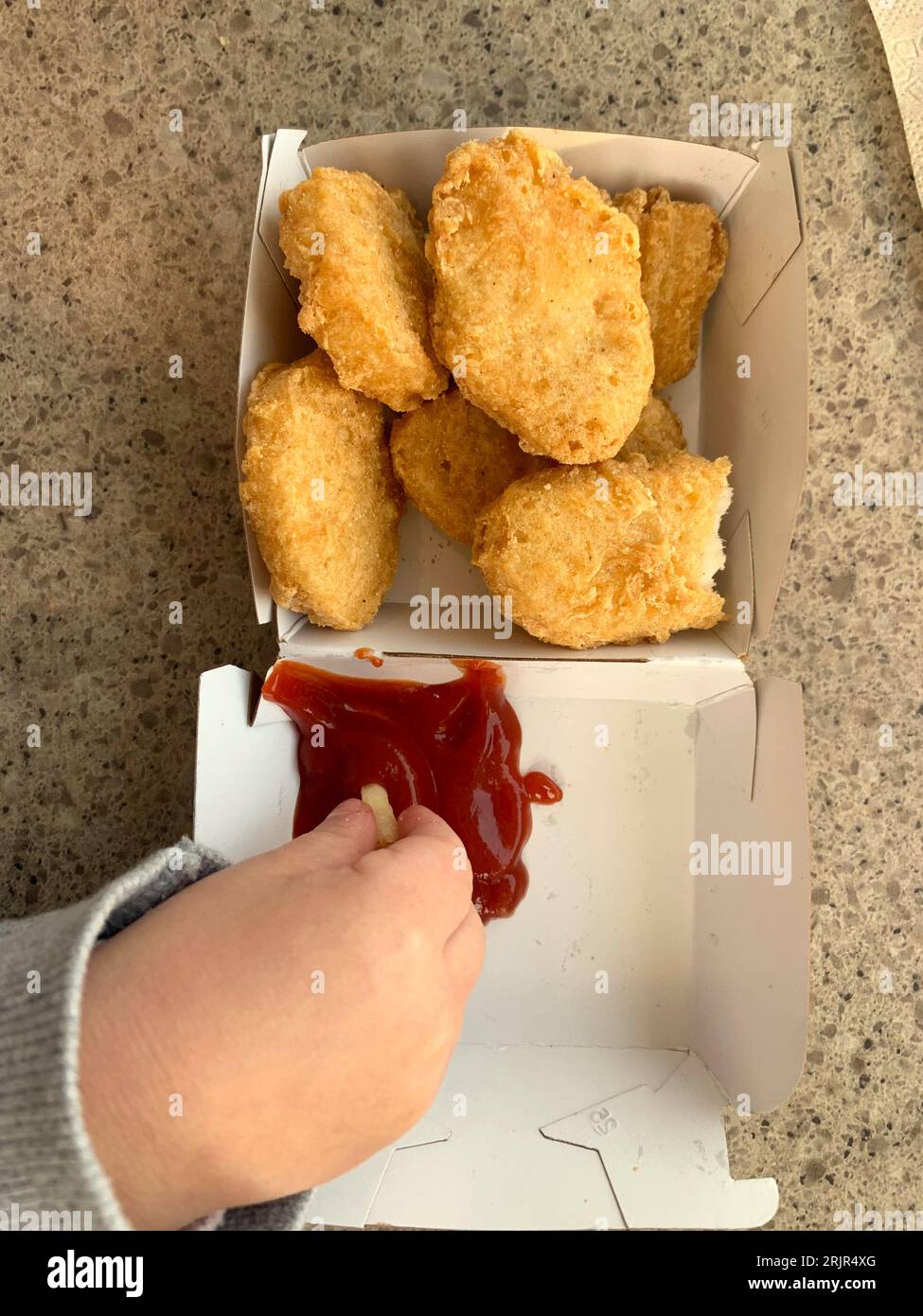 Little girl's hand dipping chicken nuggets in ketchup Stock Photo - Alamy