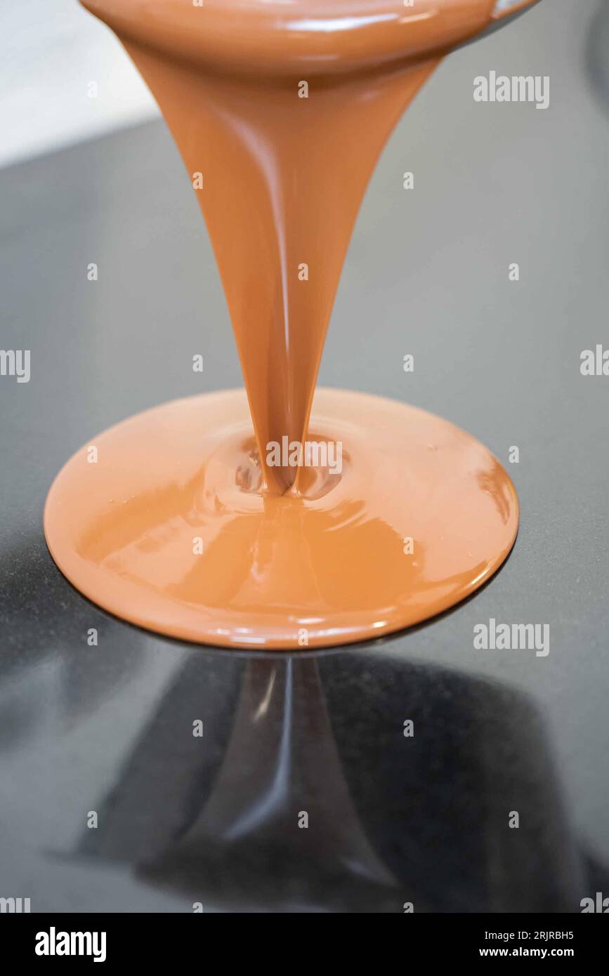 A close-up of a person pouring melted liquid chocolate onto a bowl ...