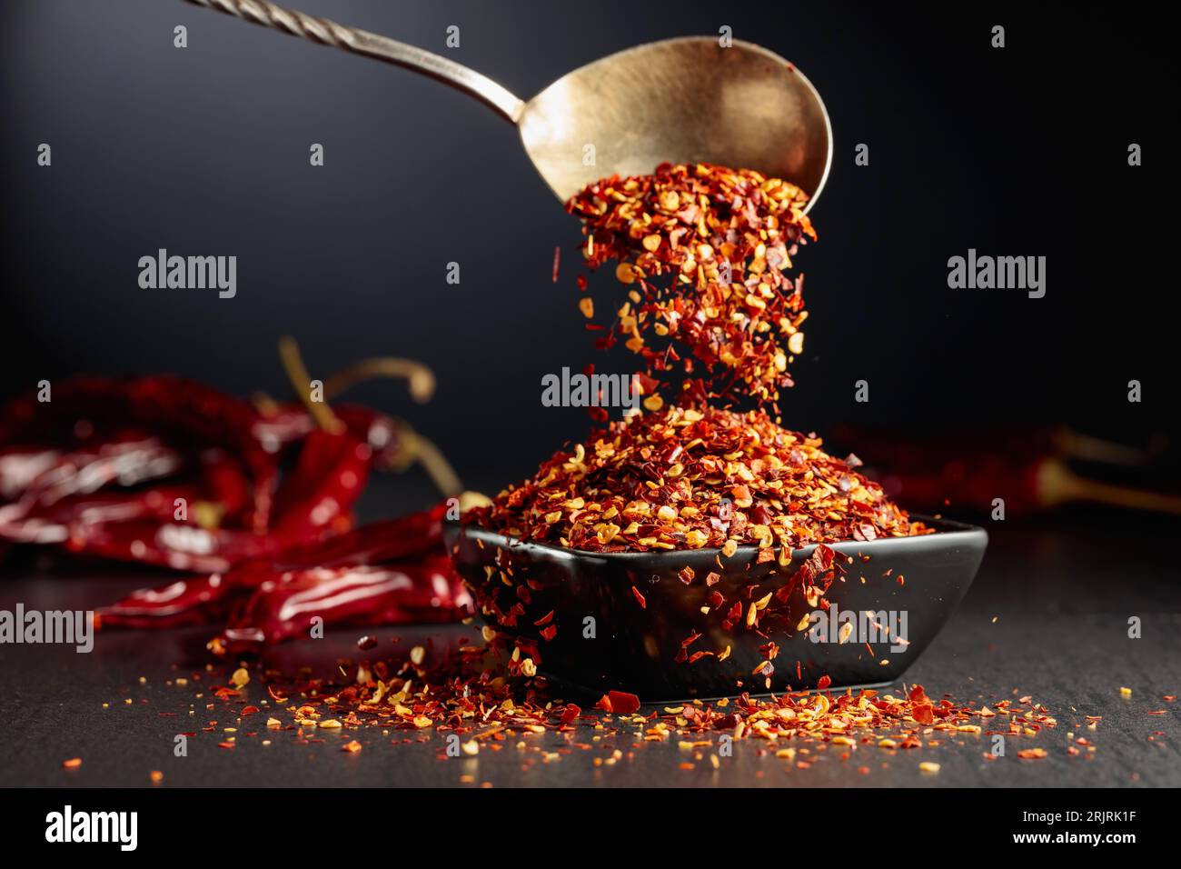Chilli flakes are poured into a black dish. Chilli flakes and dried ...