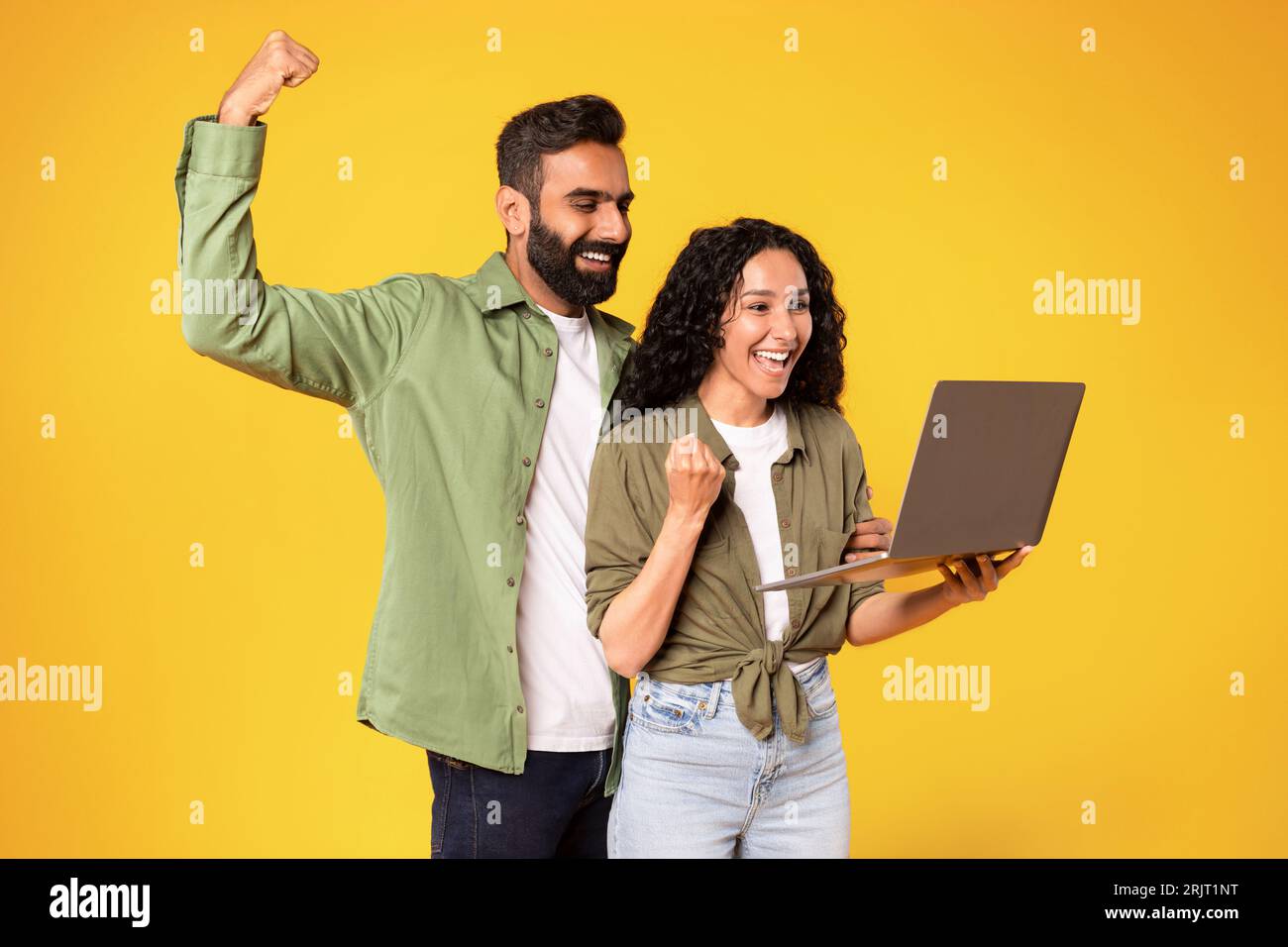 Arabic couple celebrating digital success holding laptop on yellow ...