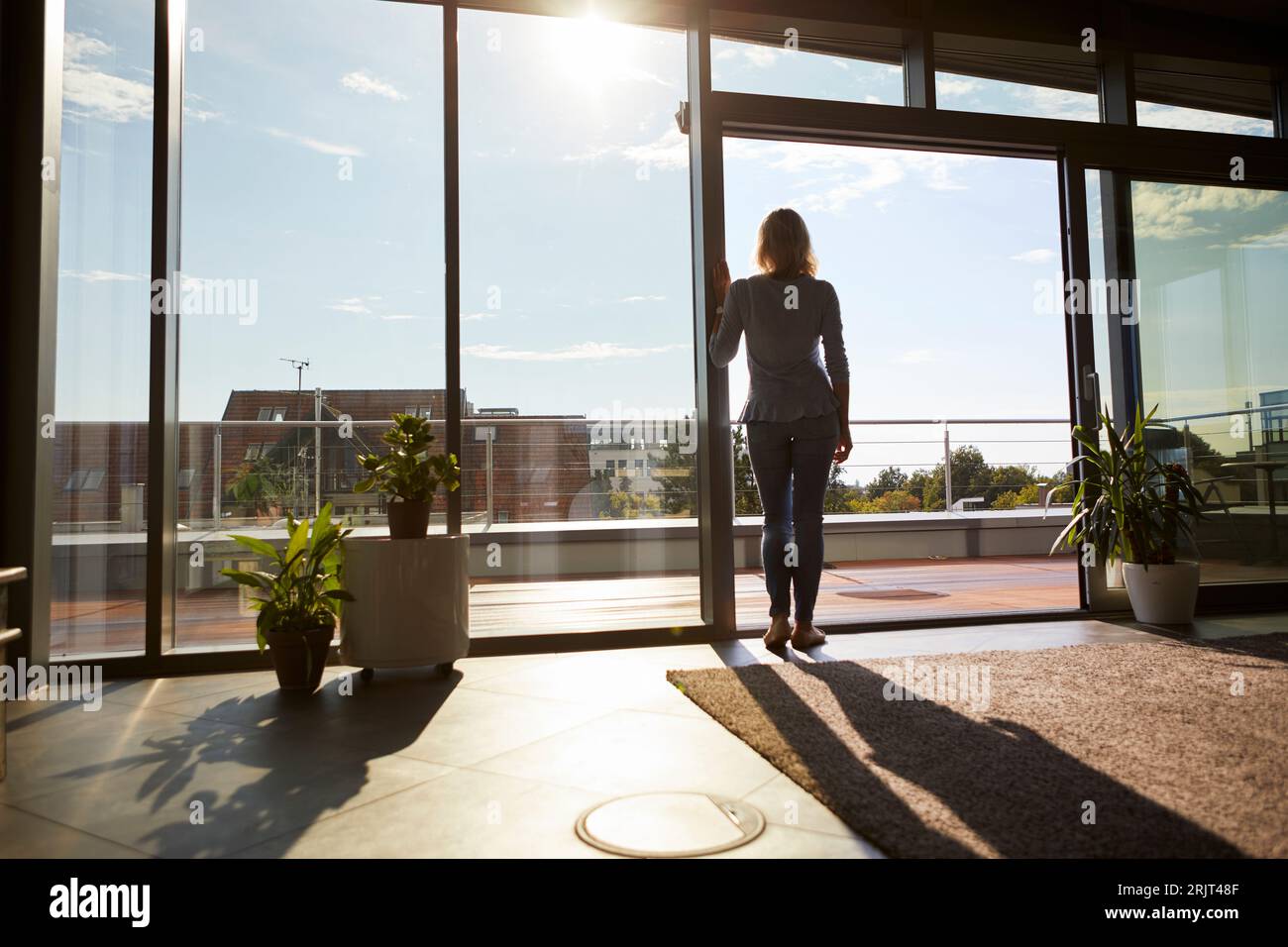 Back view woman in backlight standing at the window at home looking out ...