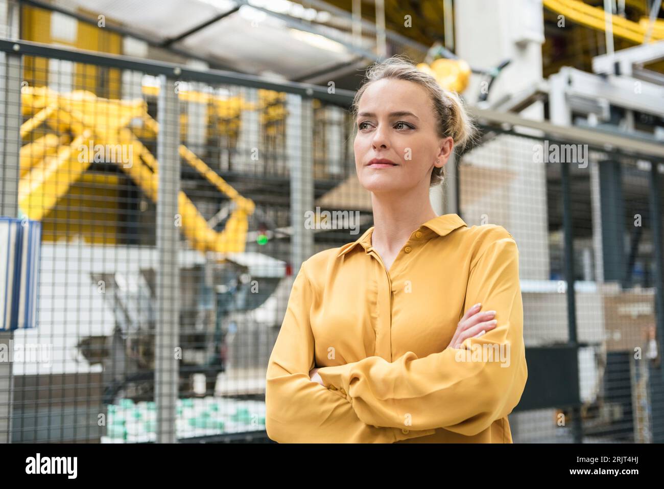 Portrait of confident woman in factory shop floor with industrial robot ...
