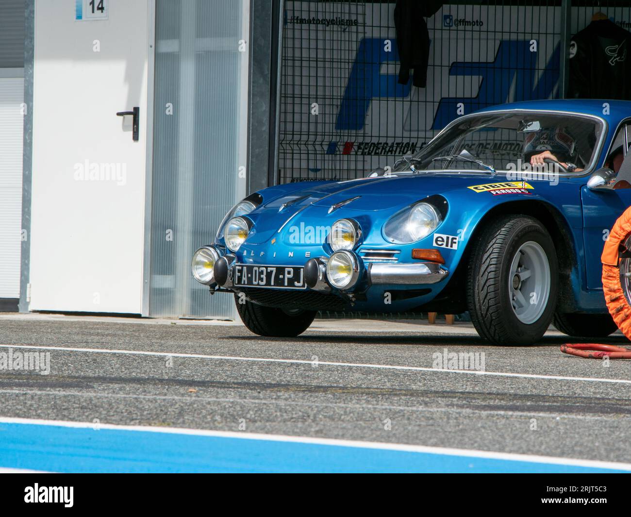 An antique blue racing vehicle is parked on a racetrack next to a red ...