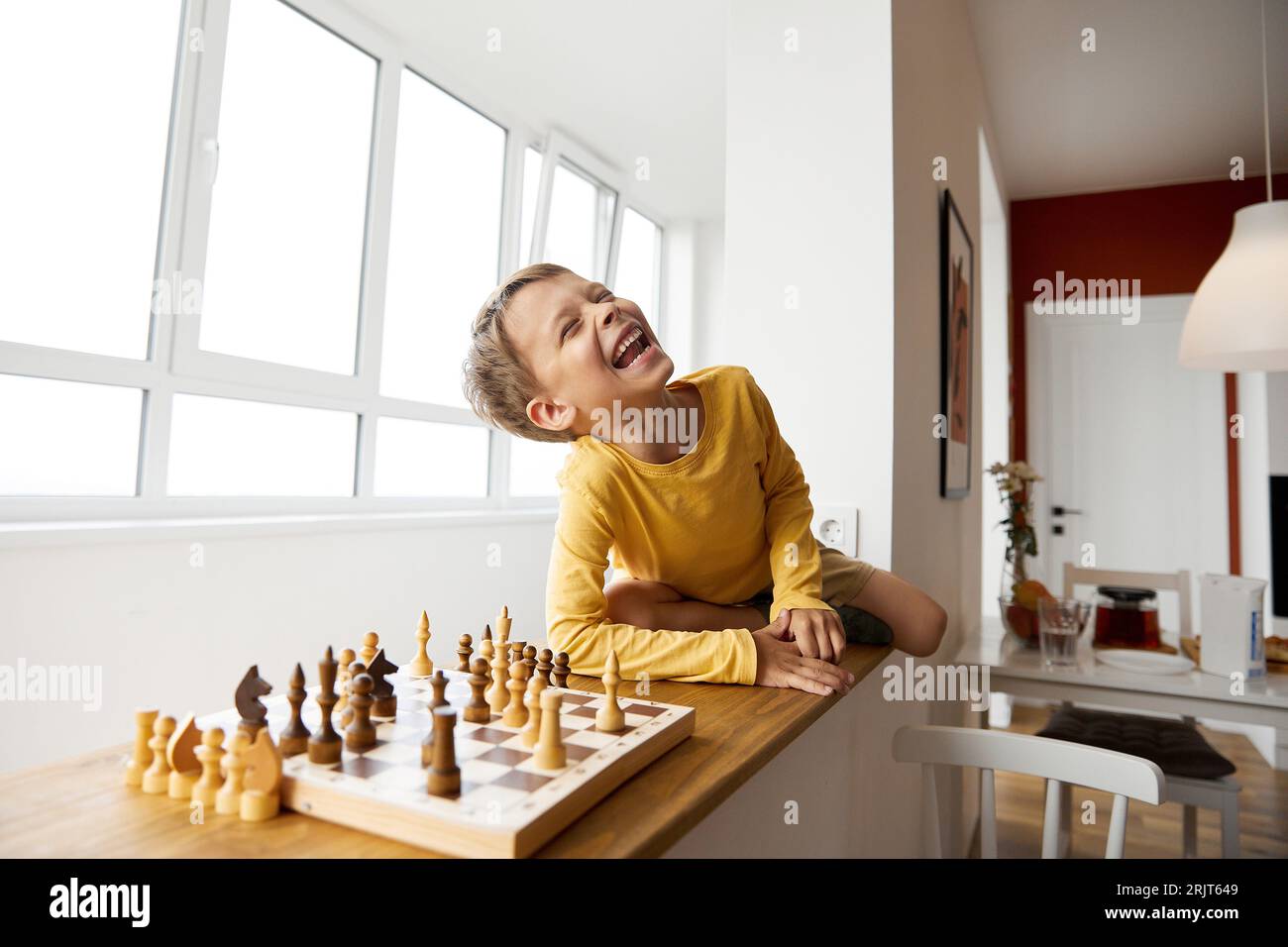 Cheerful boy playing chess and sitting on window sill at home Stock ...