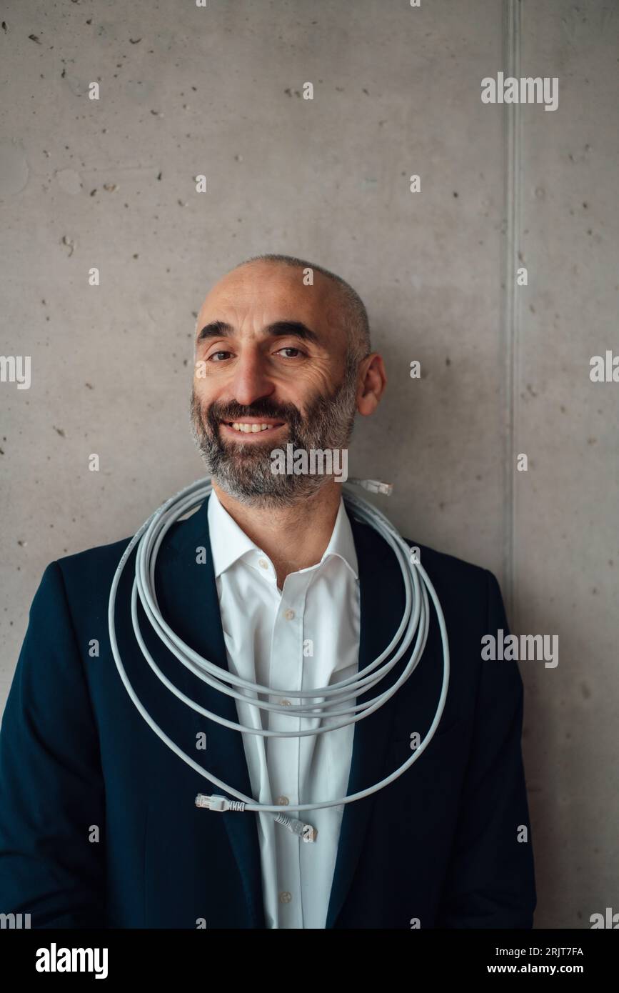 Mature businessman with computer cable around neck standing in front of ...