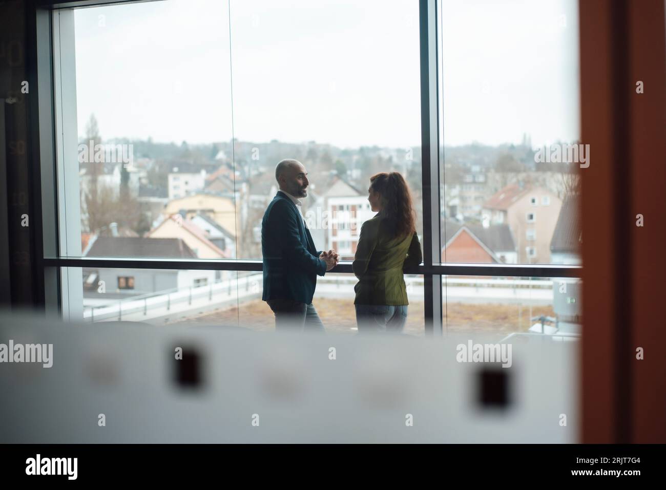Businessman talking to colleague in front of glass window Stock Photo ...