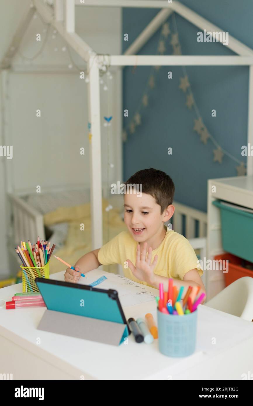 Smiling boy holding colored pencil and talking on video call through ...