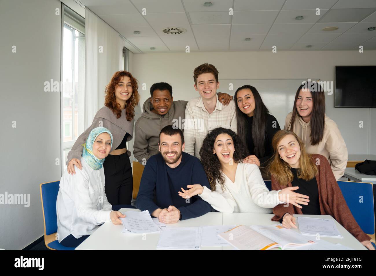 Cheerful students sitting around table with books in classroom Stock ...