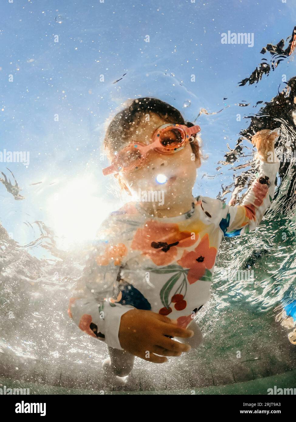 A cheerful young boy happily swimming in a clear blue pool of water ...