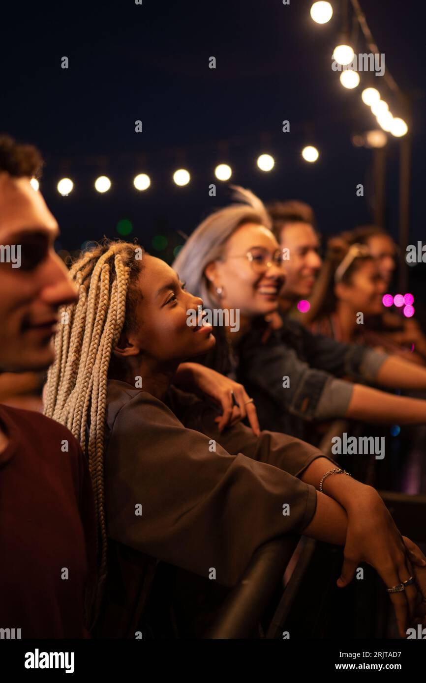 Happy friends having social gathering under string lights on rooftop ...