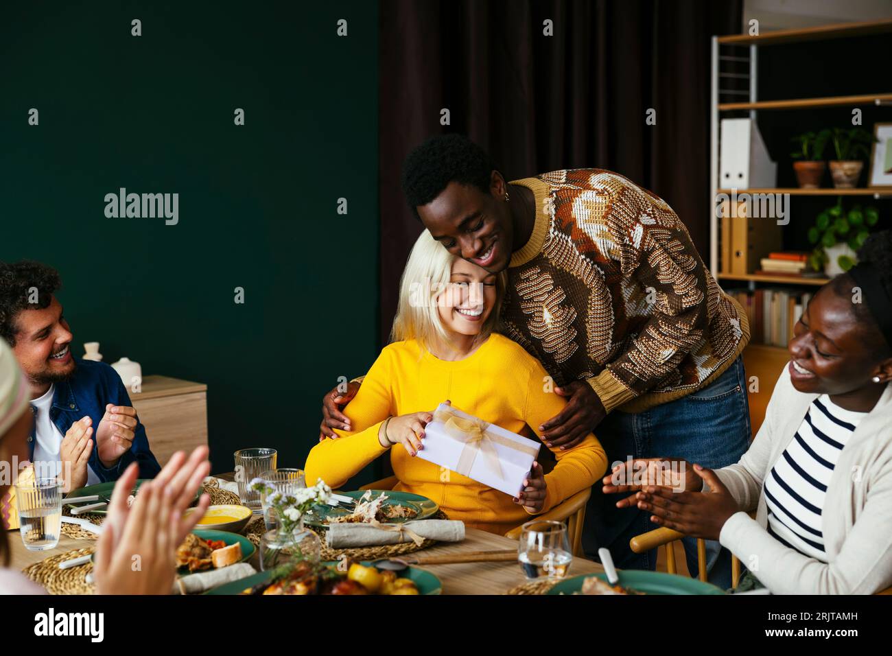 Smiling man hugging friend at dining table Stock Photo - Alamy