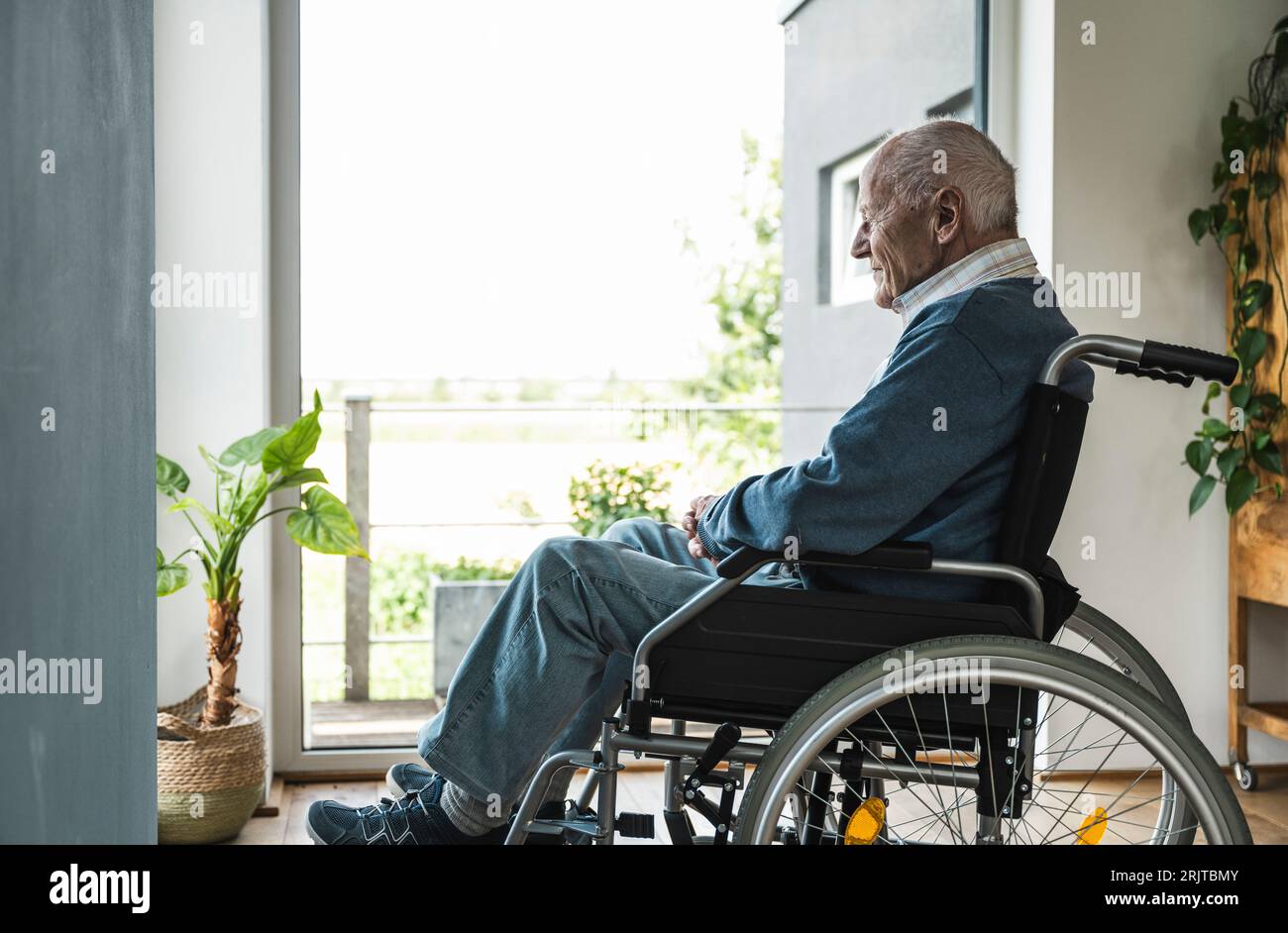 Senior man sitting in wheelchair by window at home Stock Photo - Alamy