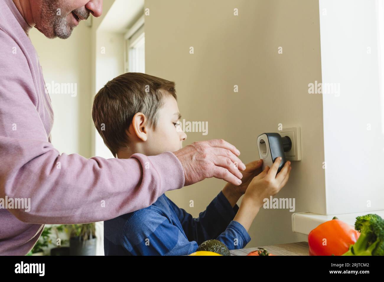Grandfather and grandson installing timer in electrical outlet on wall ...