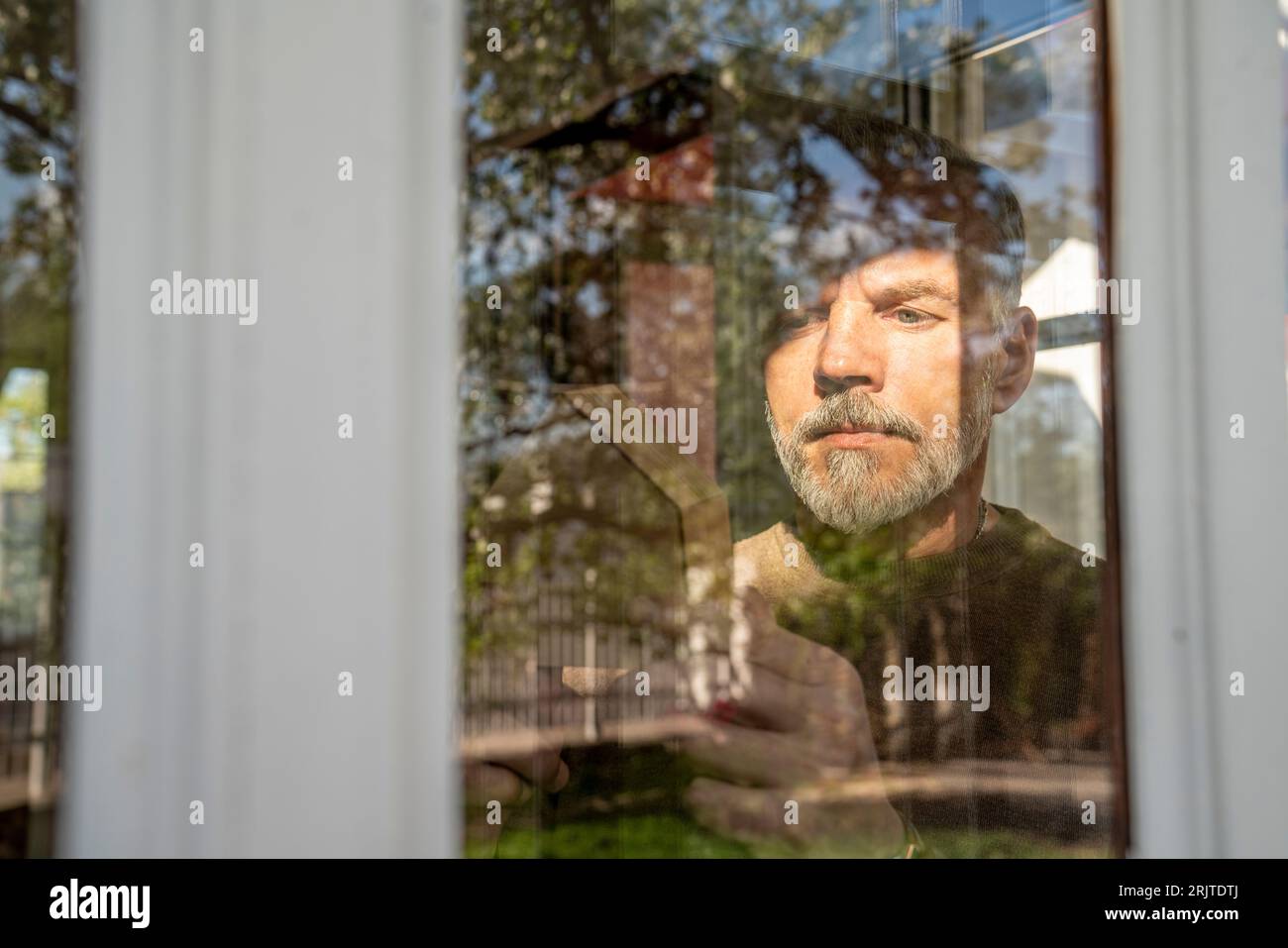 Mature man looking at house model seen through window Stock Photo - Alamy