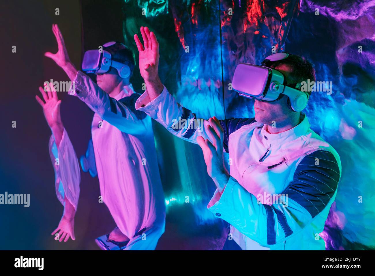 Man wearing virtual reality simulator and gesturing by mirror in neon ...
