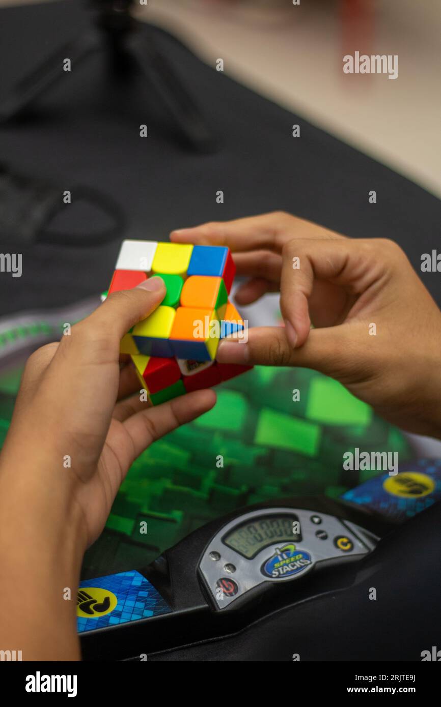 A young adult is placing a Rubik's Cube on a flat surface while holding ...