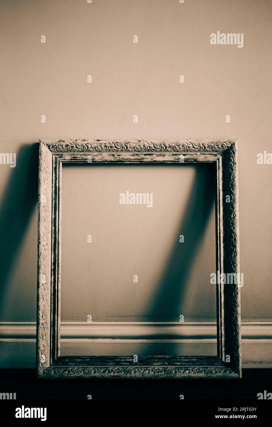 An empty, old picture frame standing next to a white wall. The closure ...