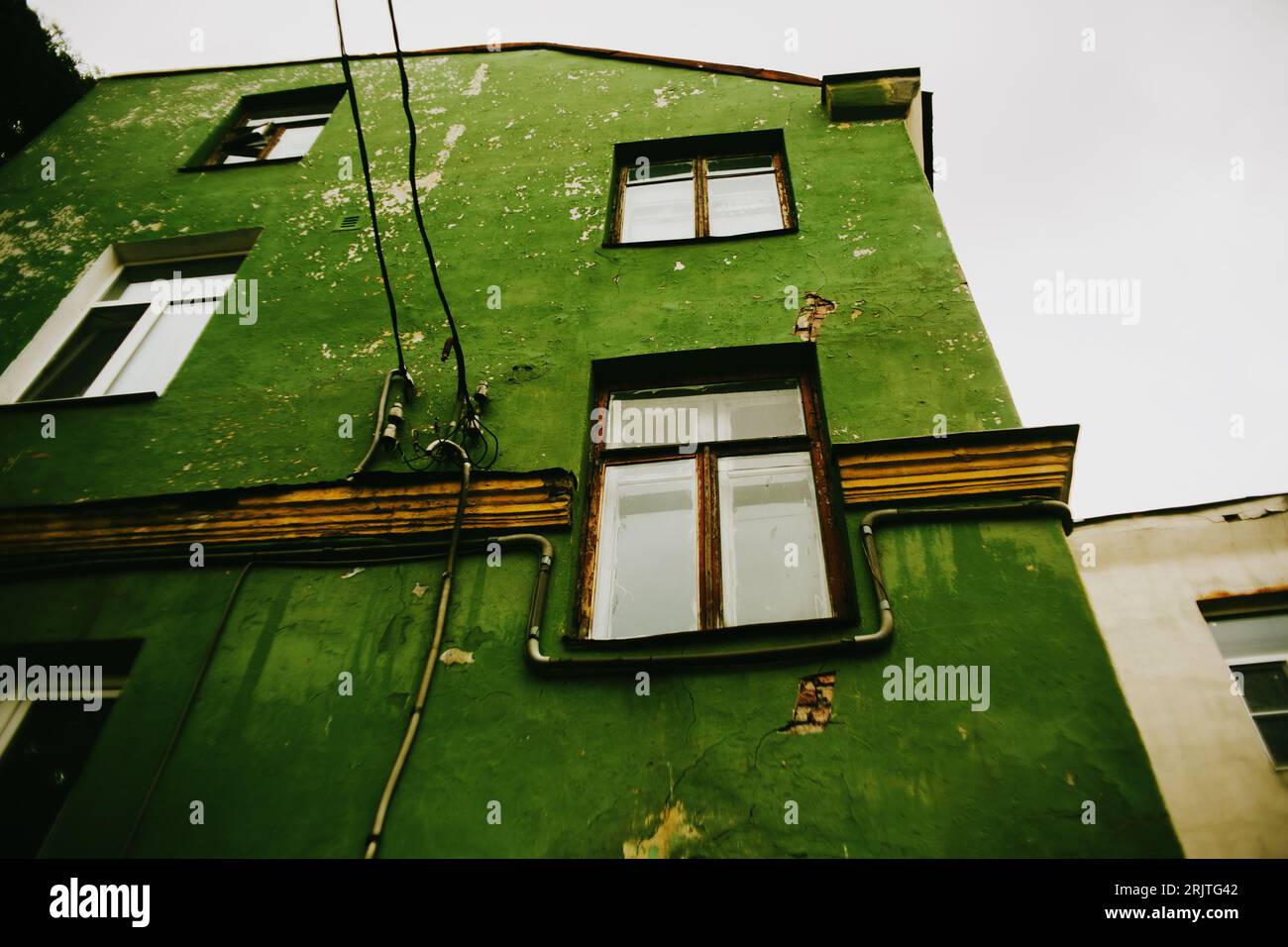 An old, shabby, green residential building on a grey day. The ...