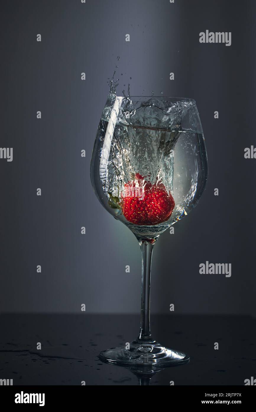 Strawberries dropped into a glass of water and splashes of water on a black table Stock Photo ...