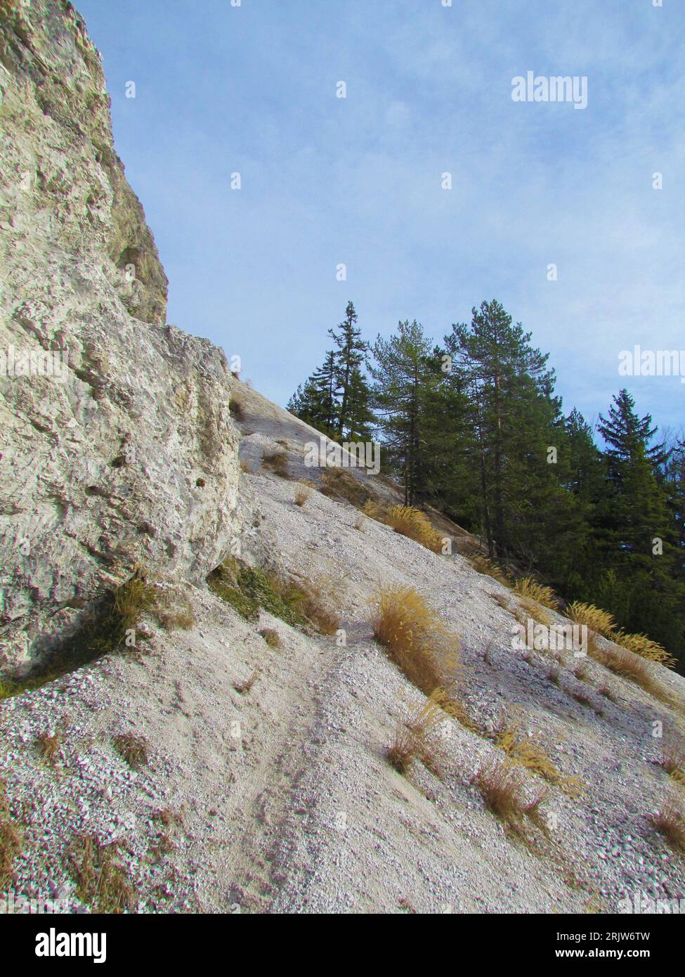 Path going under a rock wall through a scree with dry yellow grass and ...