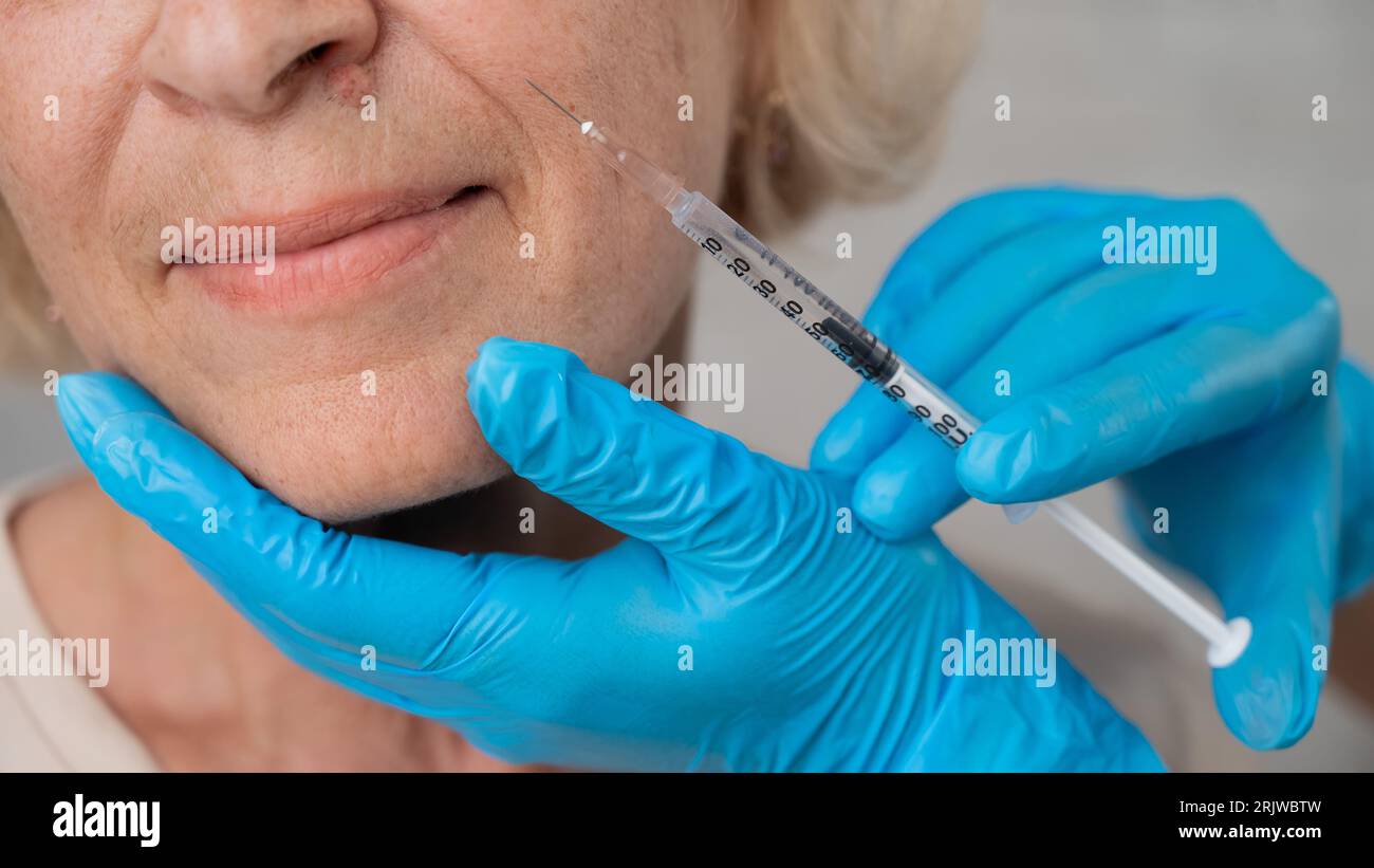 Doctor makes beauty injections in the face of an old caucasian woman ...