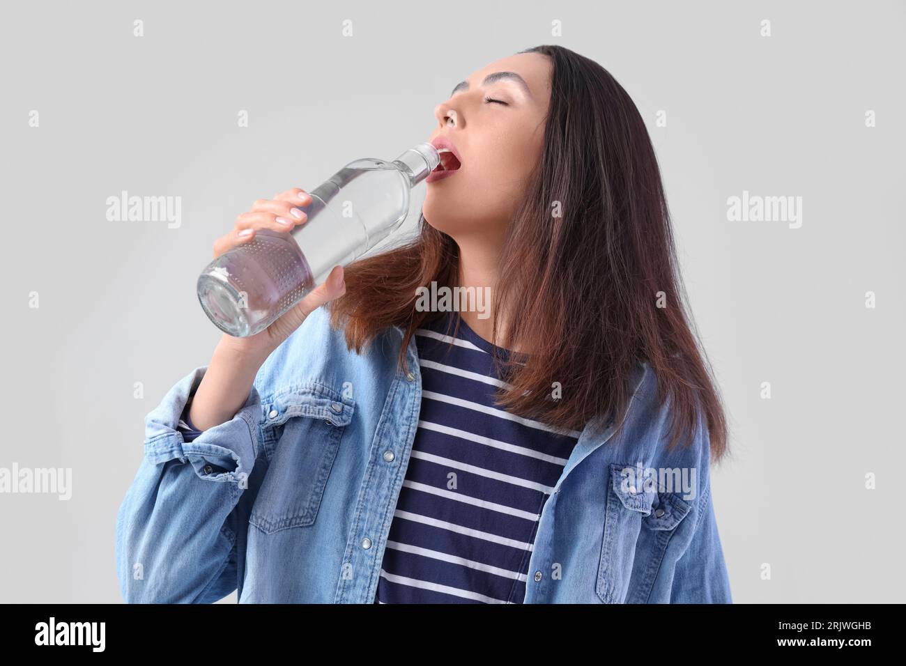 Young woman with bottle of vodka on light background Stock Photo - Alamy