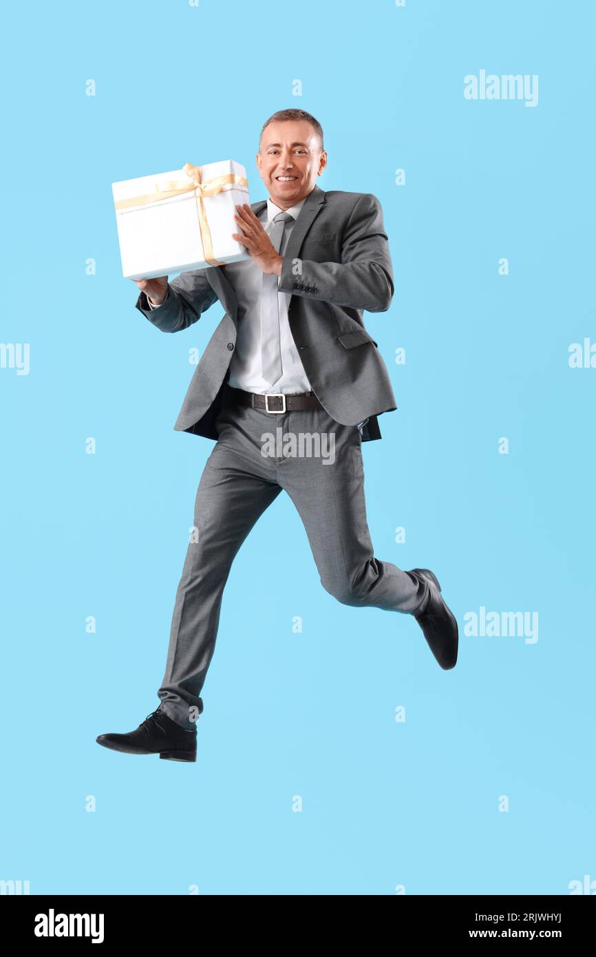 Mature businessman with birthday gift jumping on blue background Stock ...