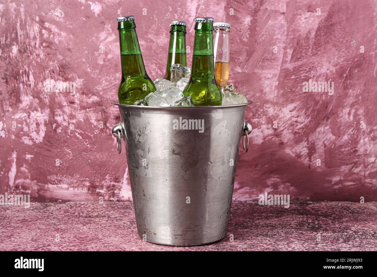 Bucket with bottles of cold beer and ice cubes on purple background ...