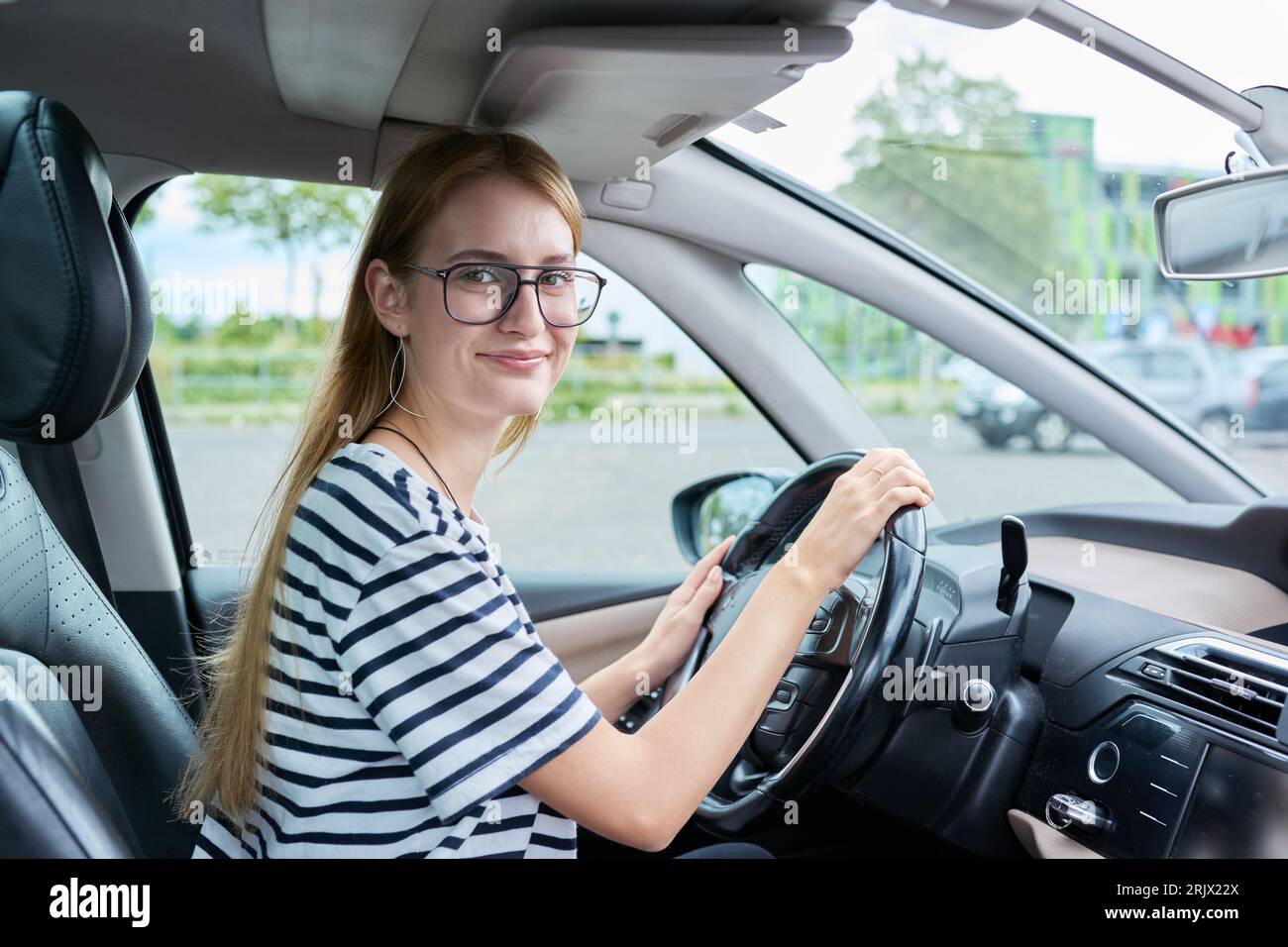 Teenage girl driver in glasses sitting behind wheel of car, looking at ...