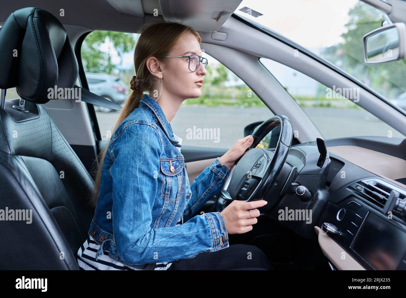 Teenage girl driver in glasses sitting behind wheel of car Stock Photo ...