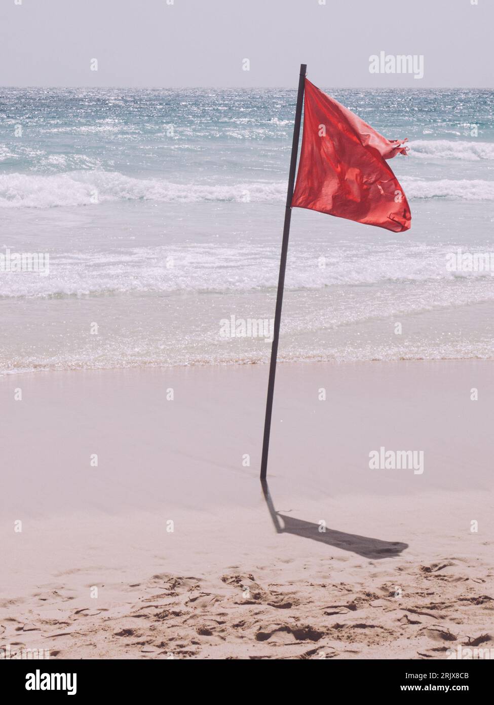 Red flag on a beach with rolling ocean waves in the background Stock ...
