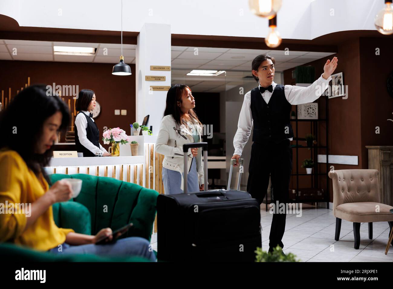 Asian male receptionist giving tourist directions to room in hallway of ...