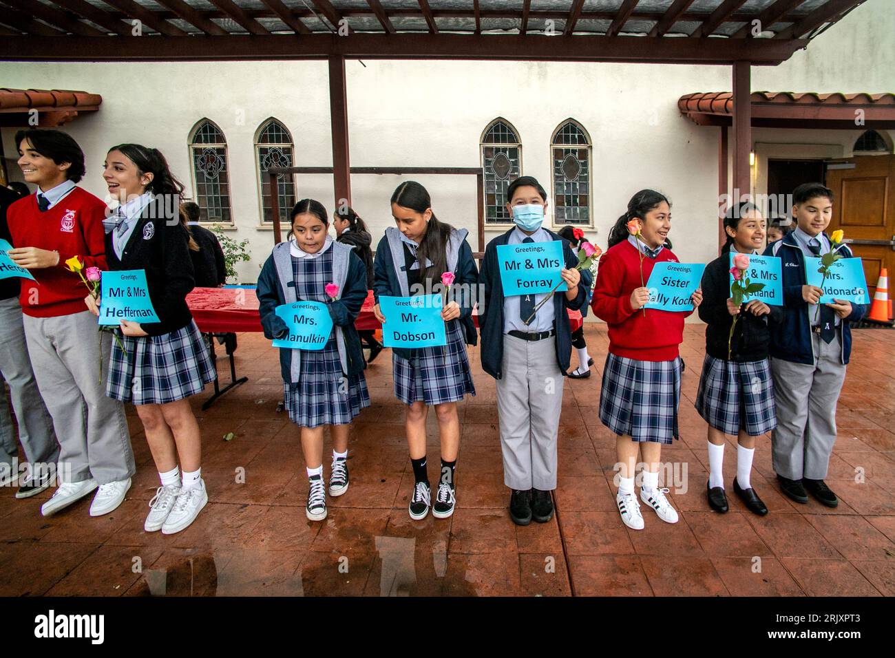 Multiracial uniformed Catholic high school students hold signs of the names of arriving ...