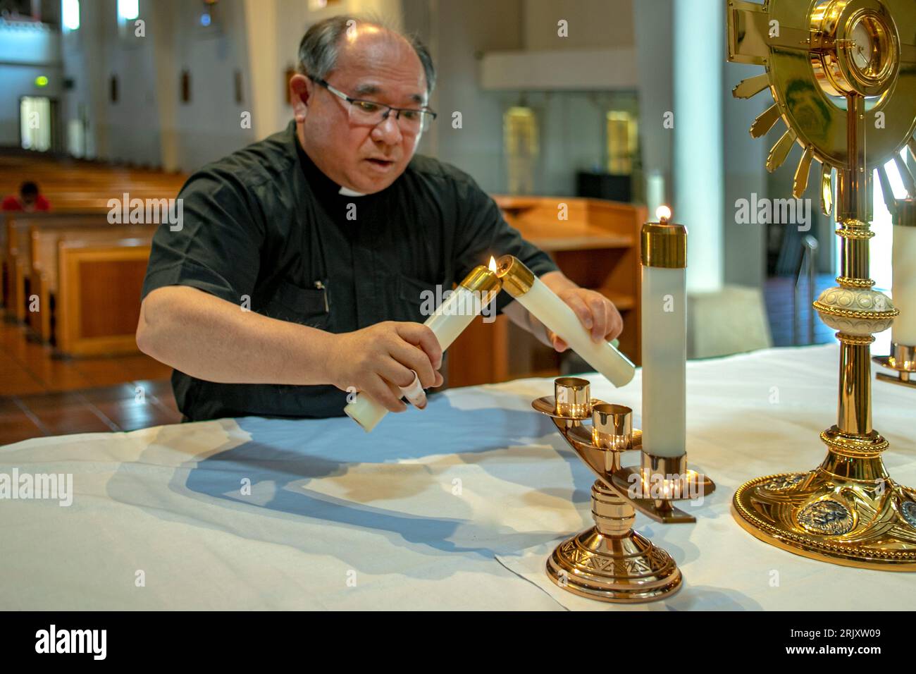 A Vietnamese American priest lights a candle on the altar of his church ...