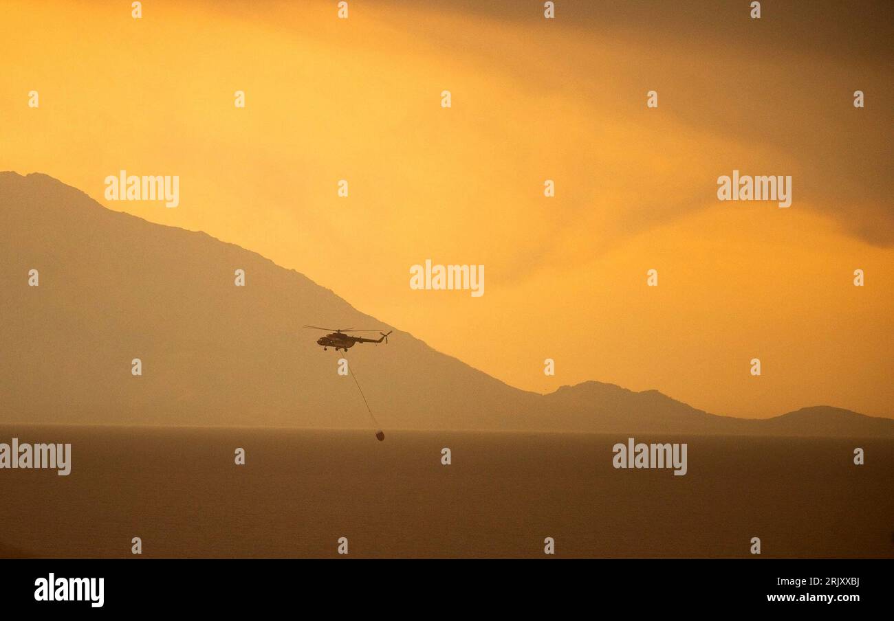 A helicopter releases water over the village of Dikela, near ...