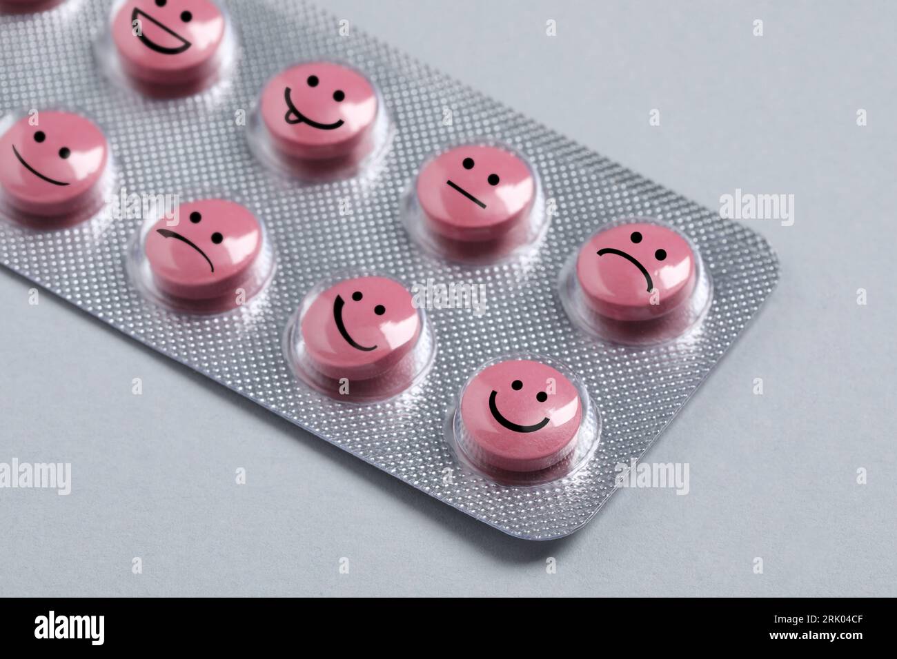 Pink pills with different emotional faces in blister on light grey ...