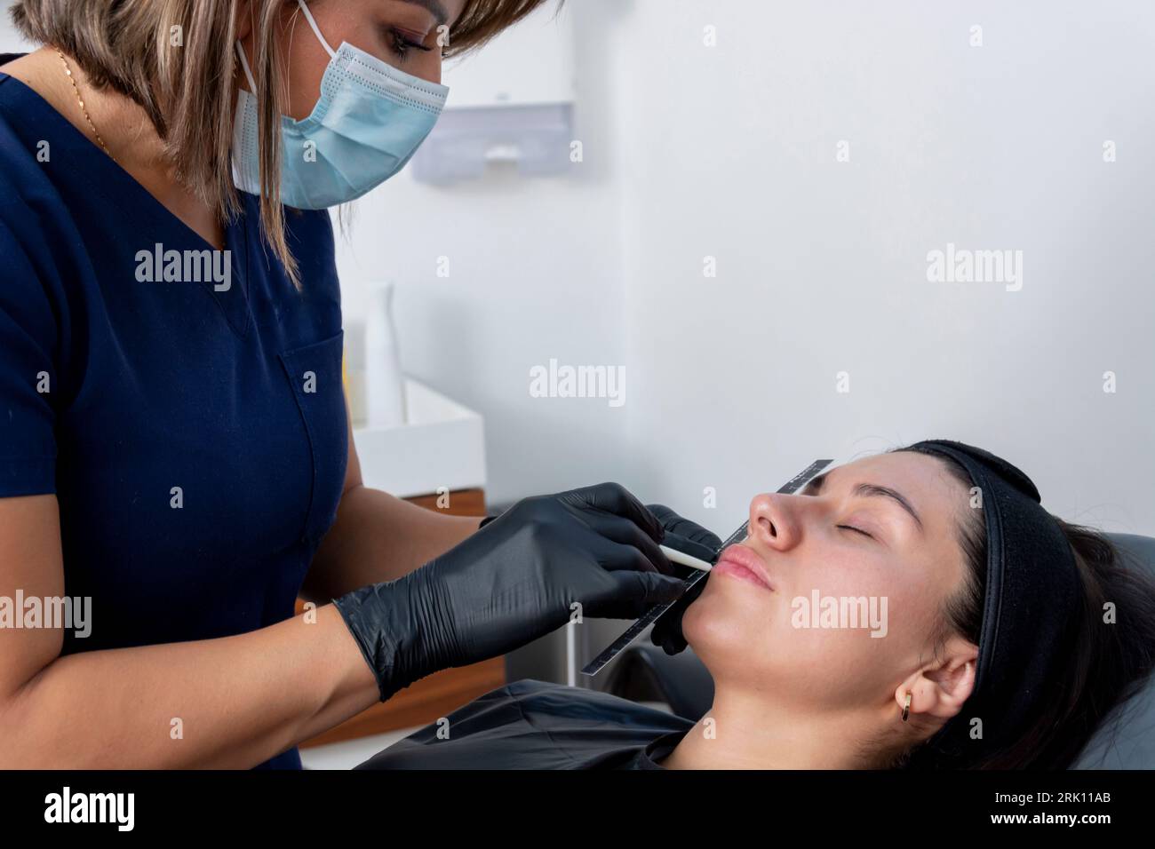 A beautician doctor measures the lips of a young woman to inject her ...